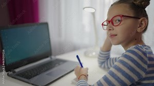 teenage girl doing homework at the laptop, looking at the screen and laughing.