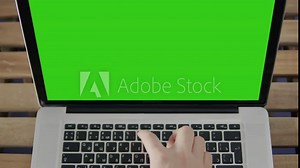 Hand of man working at laptop computer typing on keyboard on dark desktop. Close up view with green screen. 4k, top view. Laptop on wooden table. Concept of network communications or online shopping.