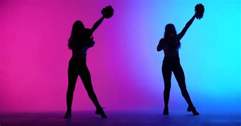 Silhouette Of Two Slender Cheerleaders Dancing Energetically With Pompoms In Hands Against