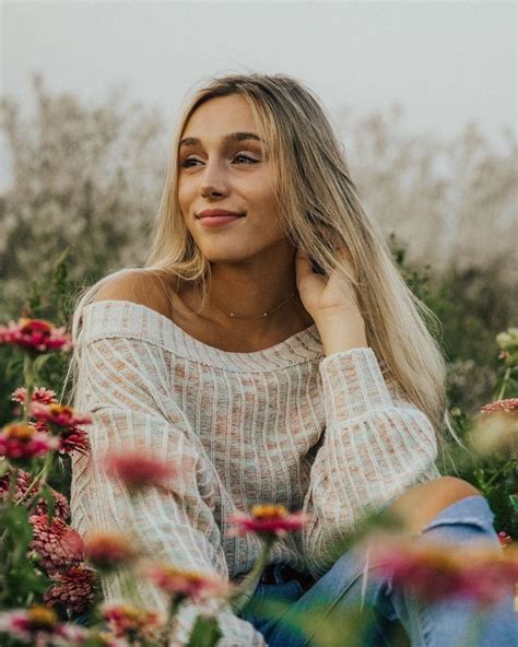 A Woman Sitting In A Field Of Flowers With Her Hand On Her Head And Looking At The Camera