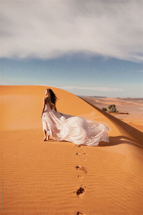 A Long Haired Brunette Woman Walking In The Desert In A Airy Wavy Pink Dress By Stocksy