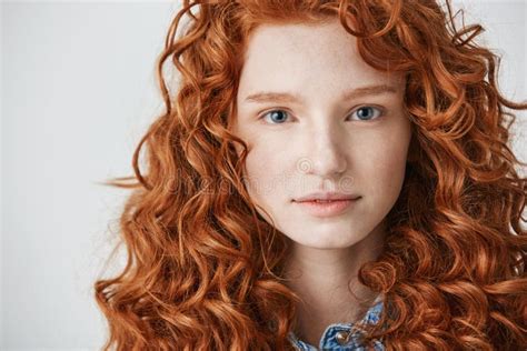 Close Up Of Beautiful Girl With Curly Red Hair And Freckles Looking At Camera Over White