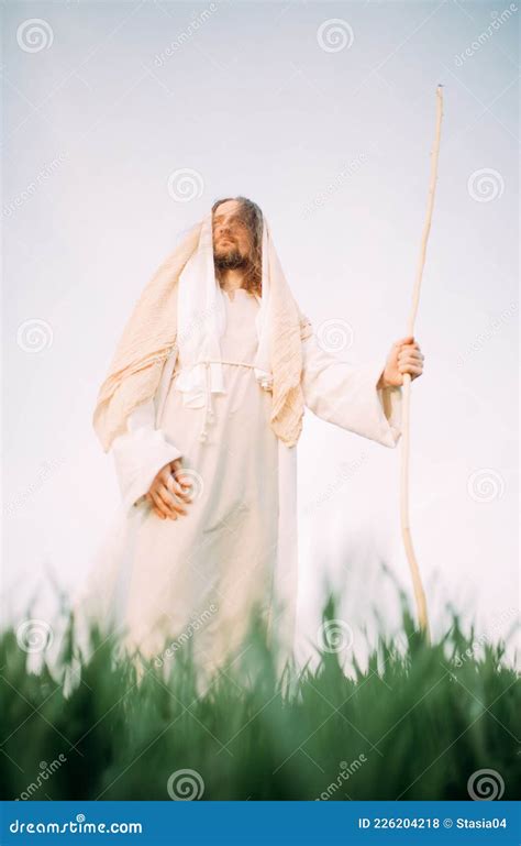 Jesus Christ With Wooden Staff Stands Clothed In White Robe Against Sky