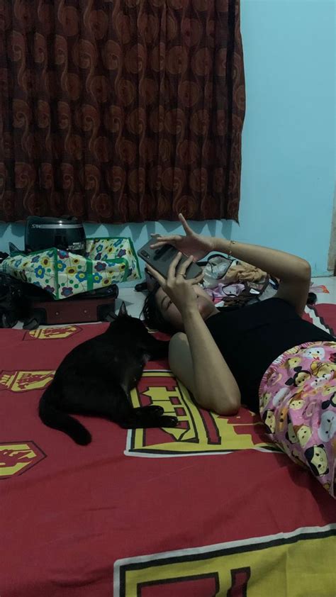 A Woman Laying On Top Of A Bed Next To A Black Cat In A Room