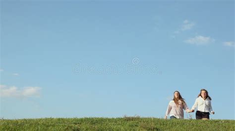 Two Young Girls Hold Hands And Walk Away By Grass Stock Footage Video Of Jeans Season 321552254