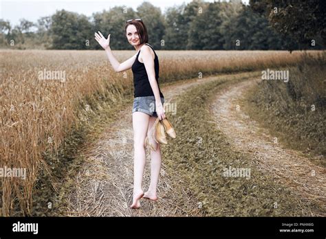 Young Girl Walking Barefoot On The Ground Road Through Field And Forest The Concept Of Summer