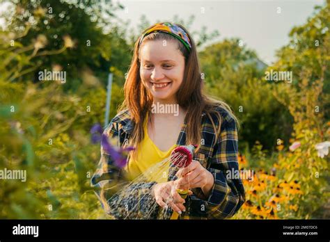 Young Pretty Girl Having Fun In The Garden Watering Plants With A Hose Smiling While Taking A