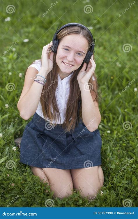 Cute Teen Girl In Headphones Enjoys The Music On The Green Grass In