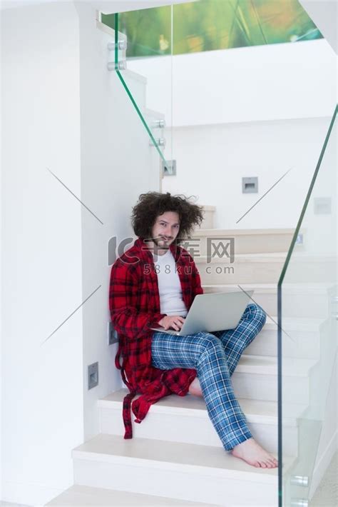 穿着浴袍的年轻自由职业者坐在楼梯上使用笔记本电脑在家工作高清摄影大图 千库网