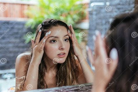 In The Bathroom At The Mirror The Girl Touches Her Face With Her Fingers Looking At Her Skin In