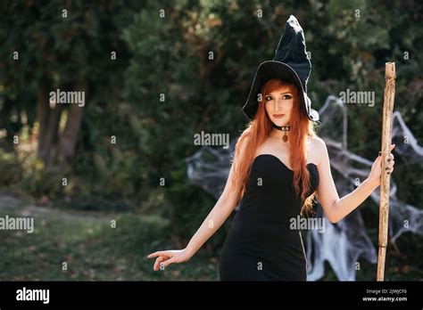 Halloween Beautiful Young Witch Girl In Witches Hat On Spooky Dark Magic Forest Background With
