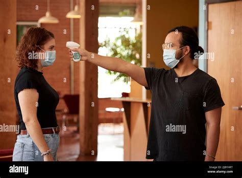 Young Caucasian Female Wearing Black T Shirt And Face Mask Having Temperature Checked With