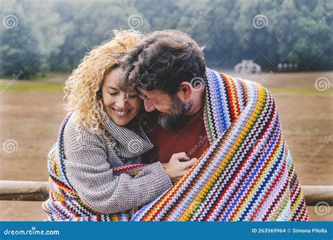 romantic adult couple in love hug with tenderness under a colorful wool cover in outdoor park