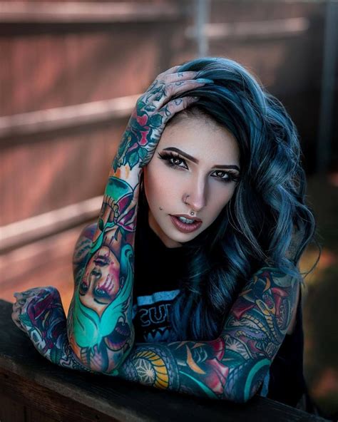 A Woman With Tattoos On Her Arms Leaning Against A Wooden Wall And