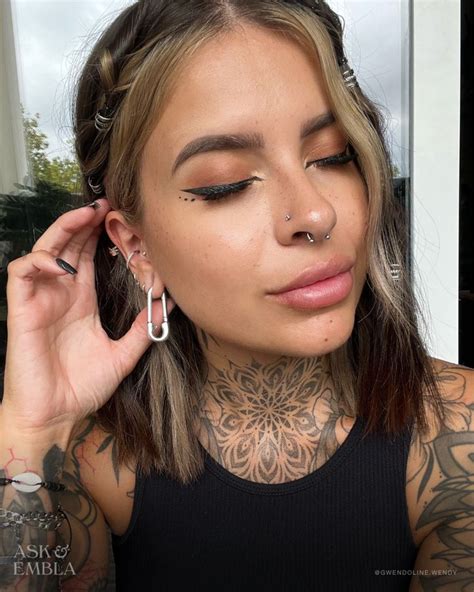 A Woman With Tattoos And Piercings On Her Neck Is Looking Down At The Camera