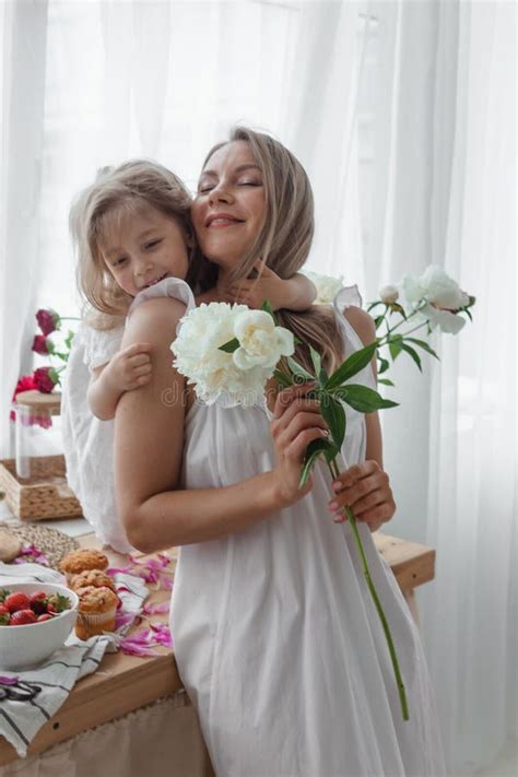 A Little Blonde Girl With Her Mom On A Kitchen Countertop Decorated With Peonies The Concept Of