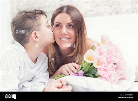 Happy Mothers Day Concept Mom With Son On Bed With T And Tulipsson Kisses His Mom Stock