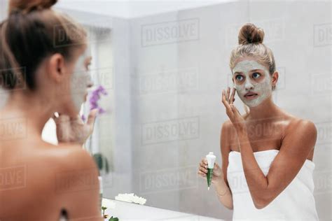 Female With Cosmetic Mask On Face In Bathroom Young Woman Applying Face Mask Infront Of Mirror