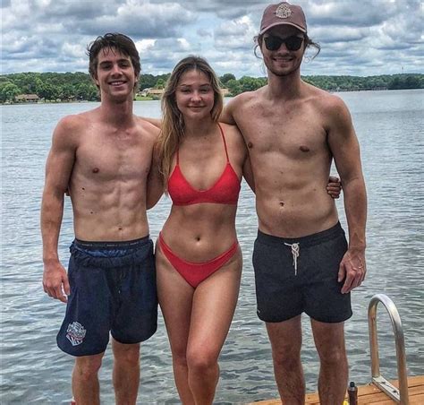 Three People Standing Next To Each Other On A Dock Near The Water And