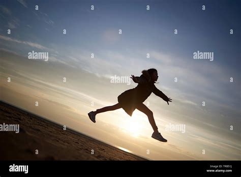 Silhouette Of A Young Girl Jumping High In The Air In A Barren Beach Landscape Making It Look As