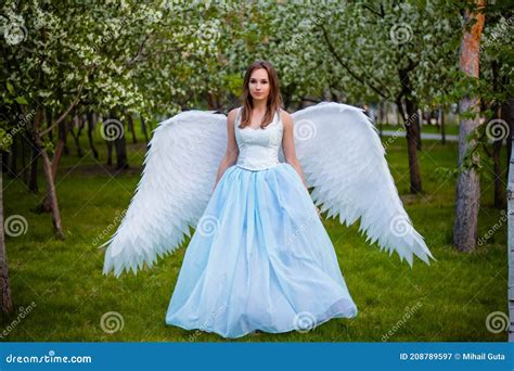 Woman In A White Corset And Blue Lush Dress With Large White Angel Wings Behind Her Back Stock