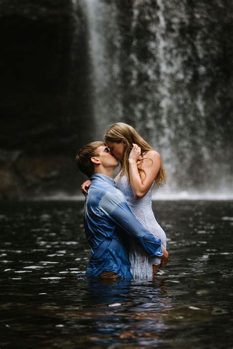 A Man And Woman Are Kissing In Front Of A Waterfall While Standing In The Water