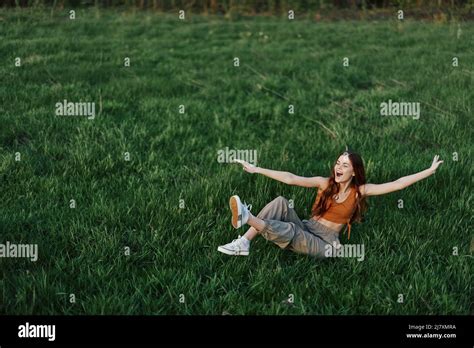 Young Woman Playing Games In The Park On The Green Grass Spreading Her Arms And Legs In